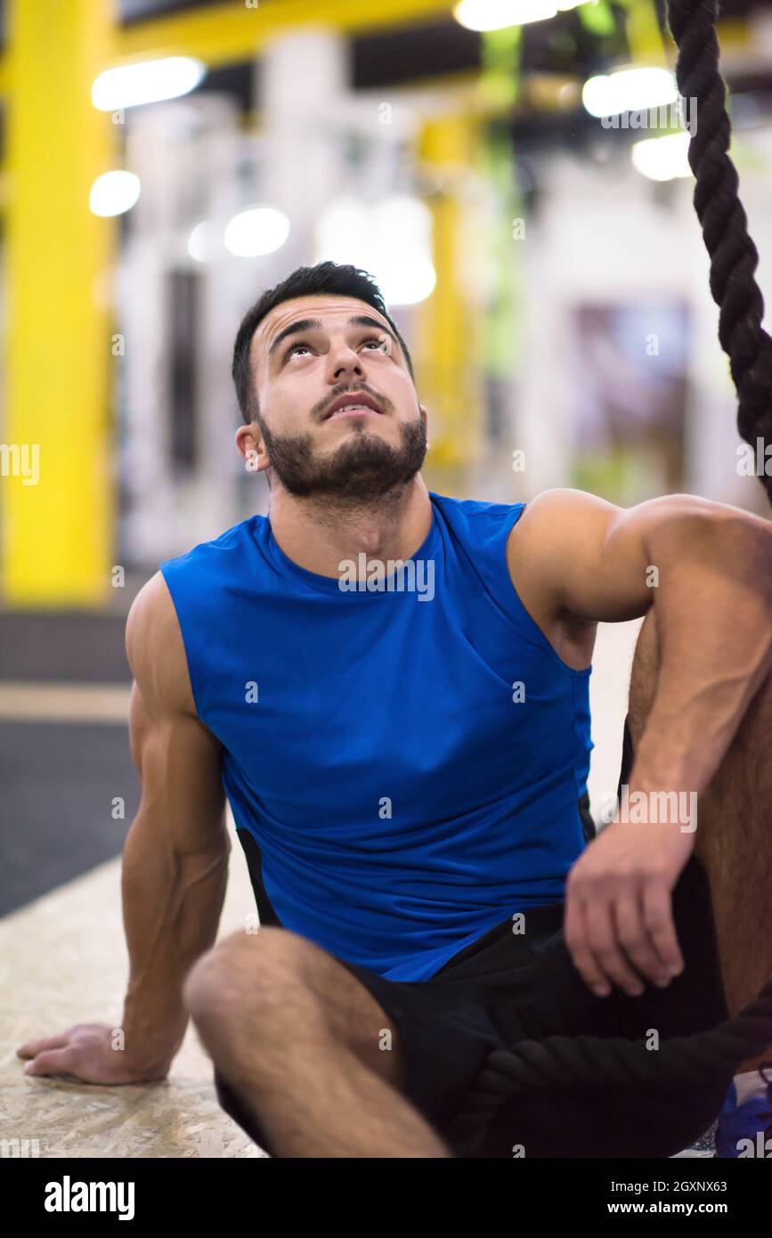 young muscular man sitting and relaxing before rope climbing in cross ...