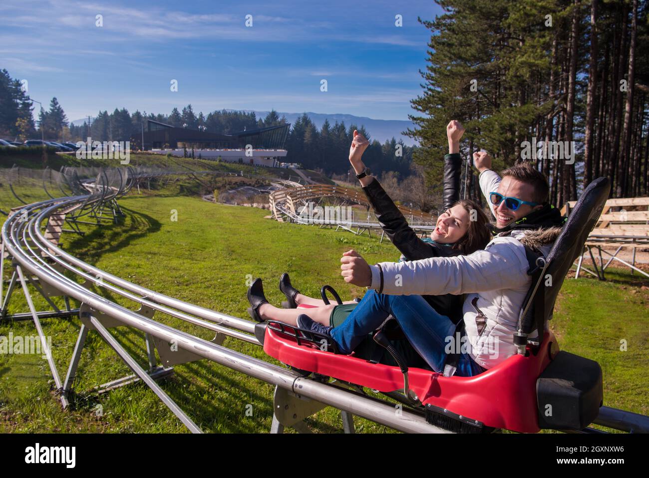 Excited young couple driving alpine coaster while enjoying beautiful ...