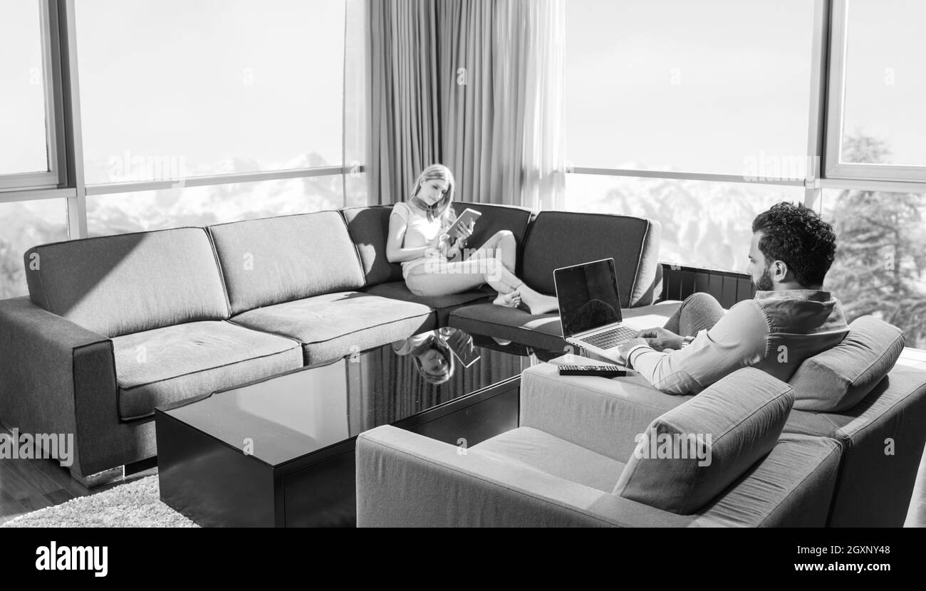 Young couple relaxing at home using tablet and laptop computers reading ...