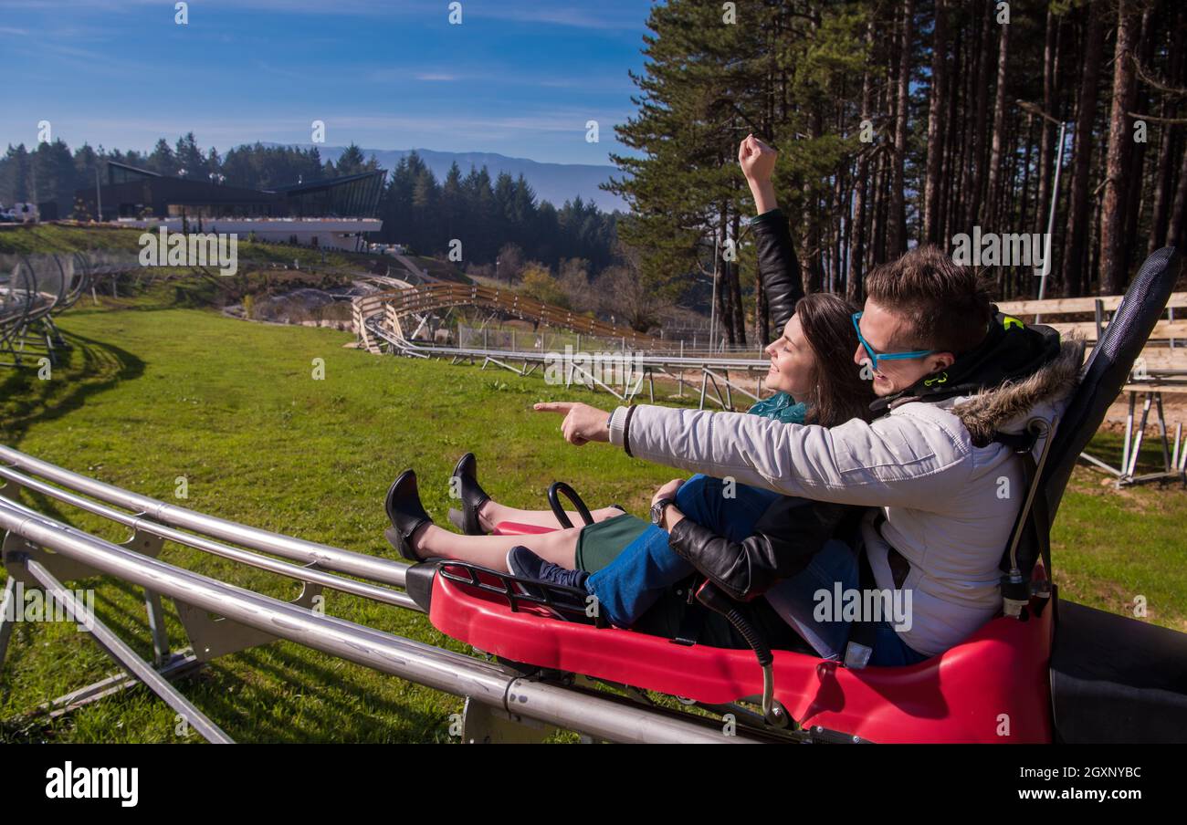 Excited young couple driving alpine coaster while enjoying beautiful ...