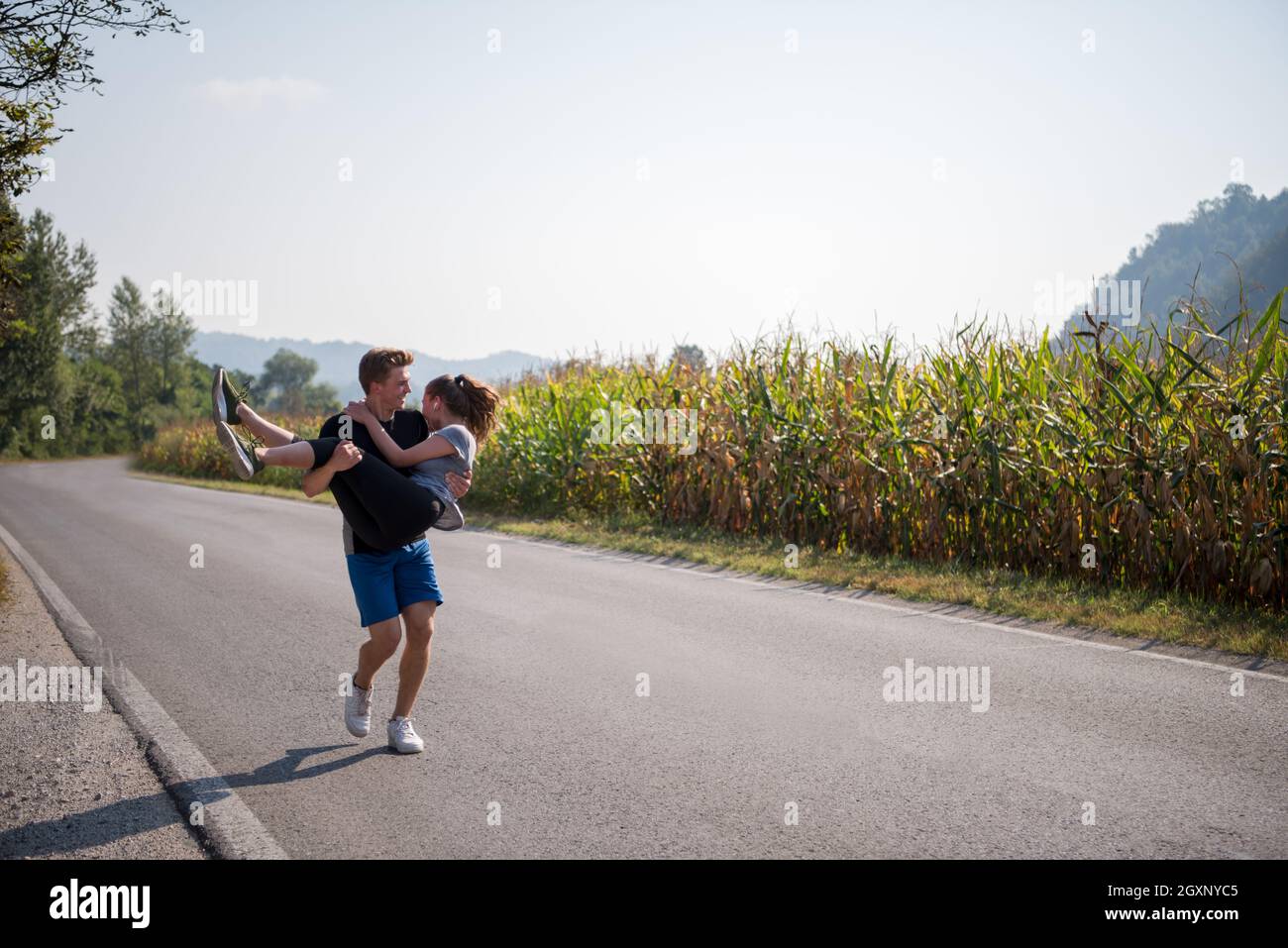 man carries a woman in his arms while jogging along a country road ...