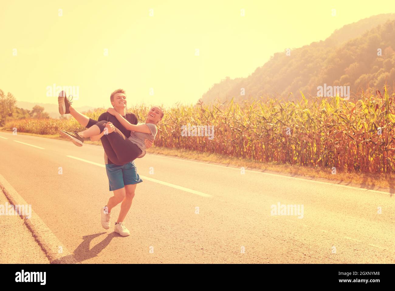 man carries a woman in his arms while jogging along a country road ...