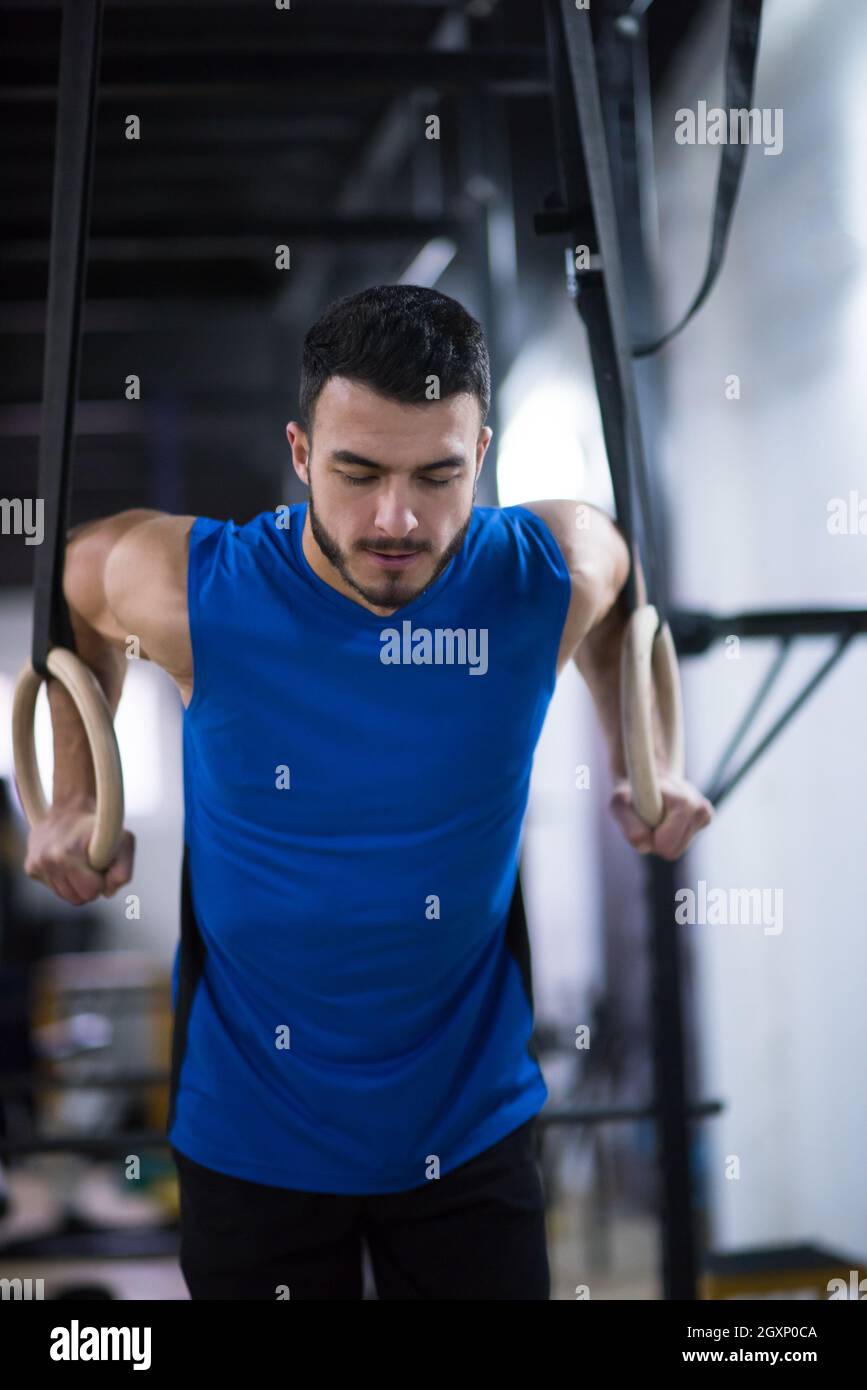 young athlete man working out pull ups with gymnastic rings at the ...