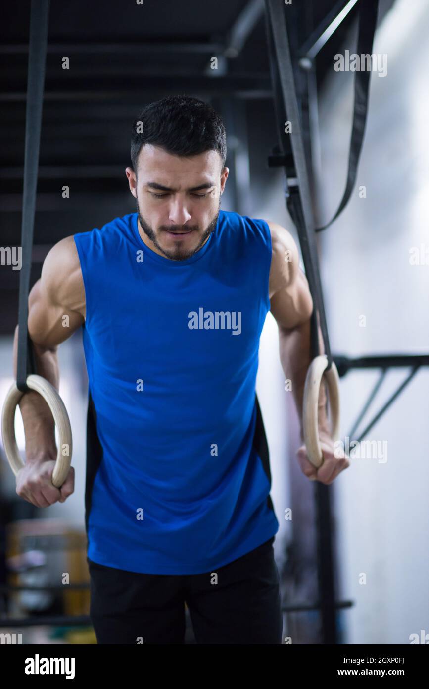 young athlete man working out pull ups with gymnastic rings at the ...