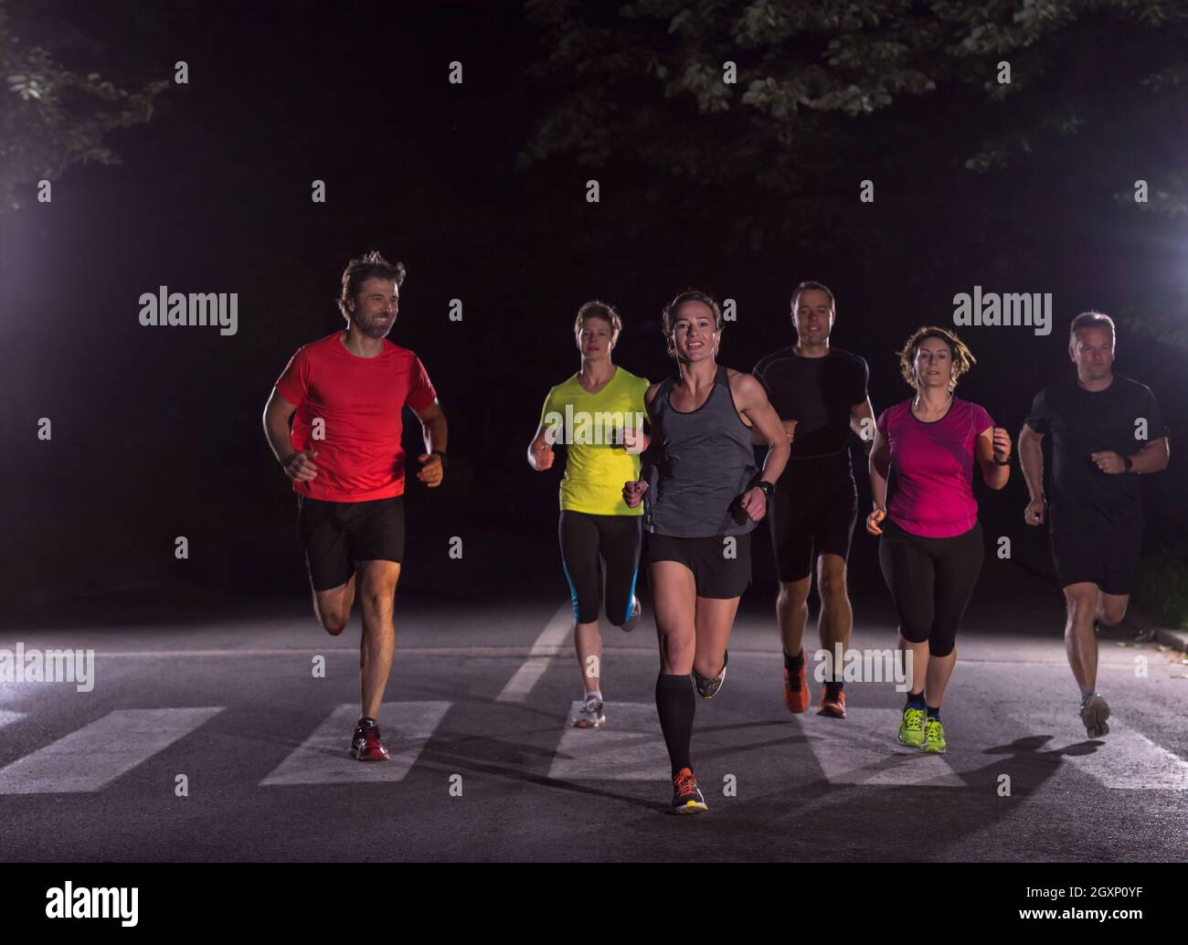 group of healthy people jogging in city park, runners team at night ...