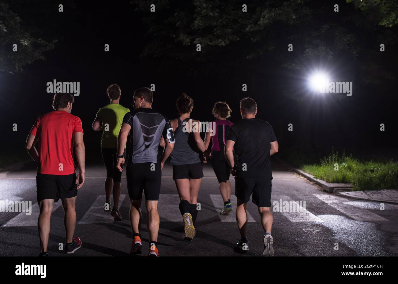 group of healthy people jogging in city park, runners team at night ...