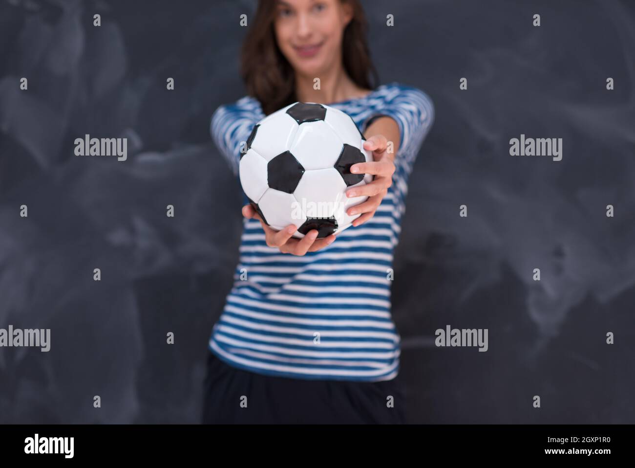 portrait of a young woman holding a soccer ball in front of chalk ...