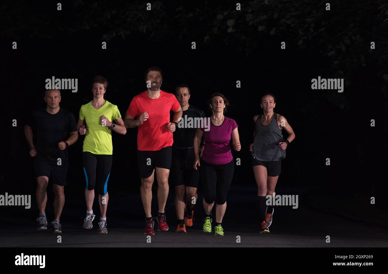group of healthy people jogging in city park, runners team at night ...