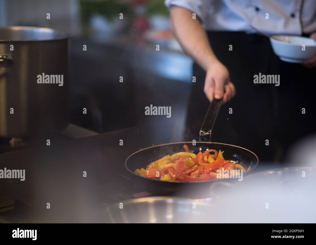 Young male chef flipping vegetables in wok at commercial kitchen Stock ...