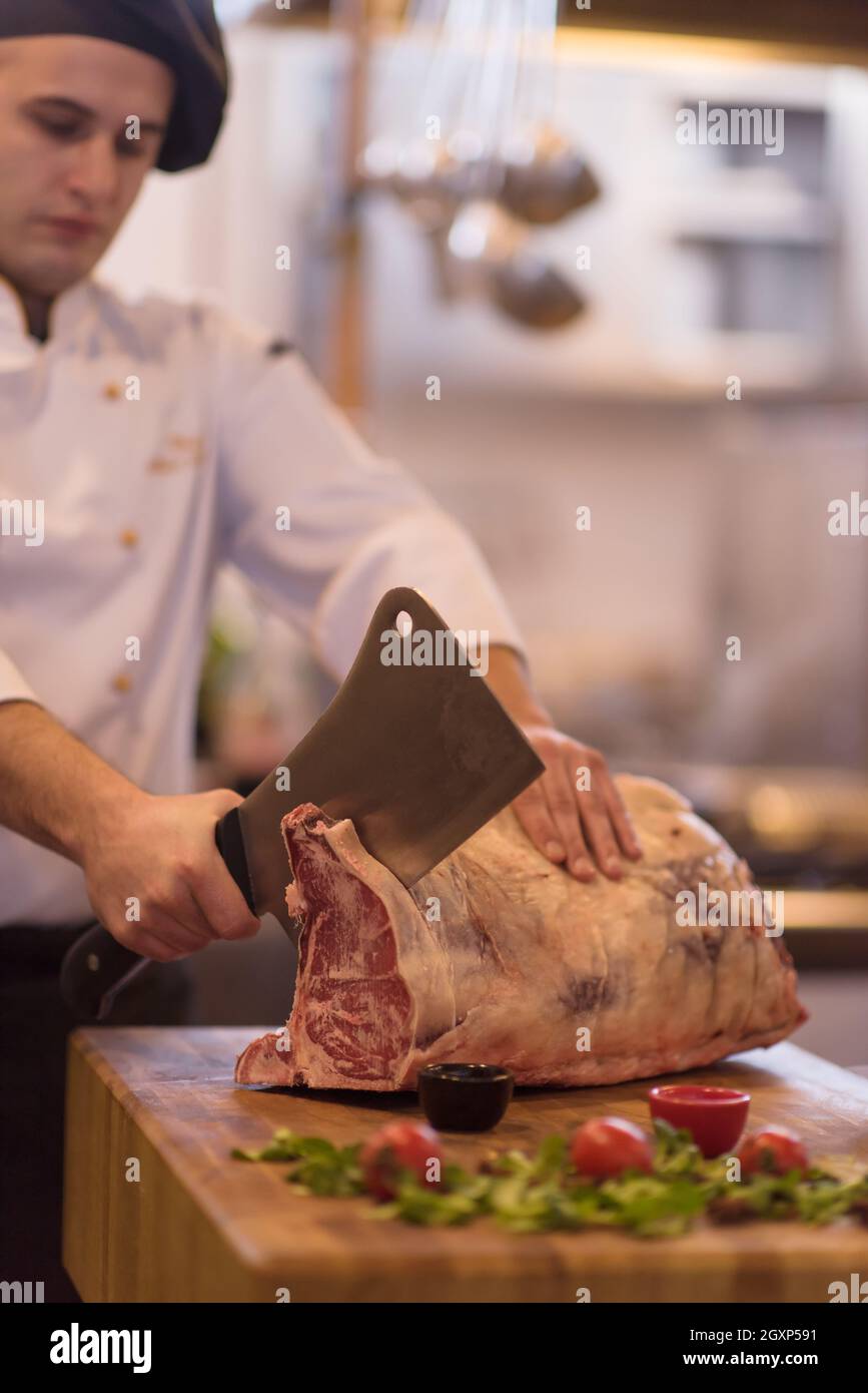 chef using ax while cutting big piece of beef on wooden board in ...