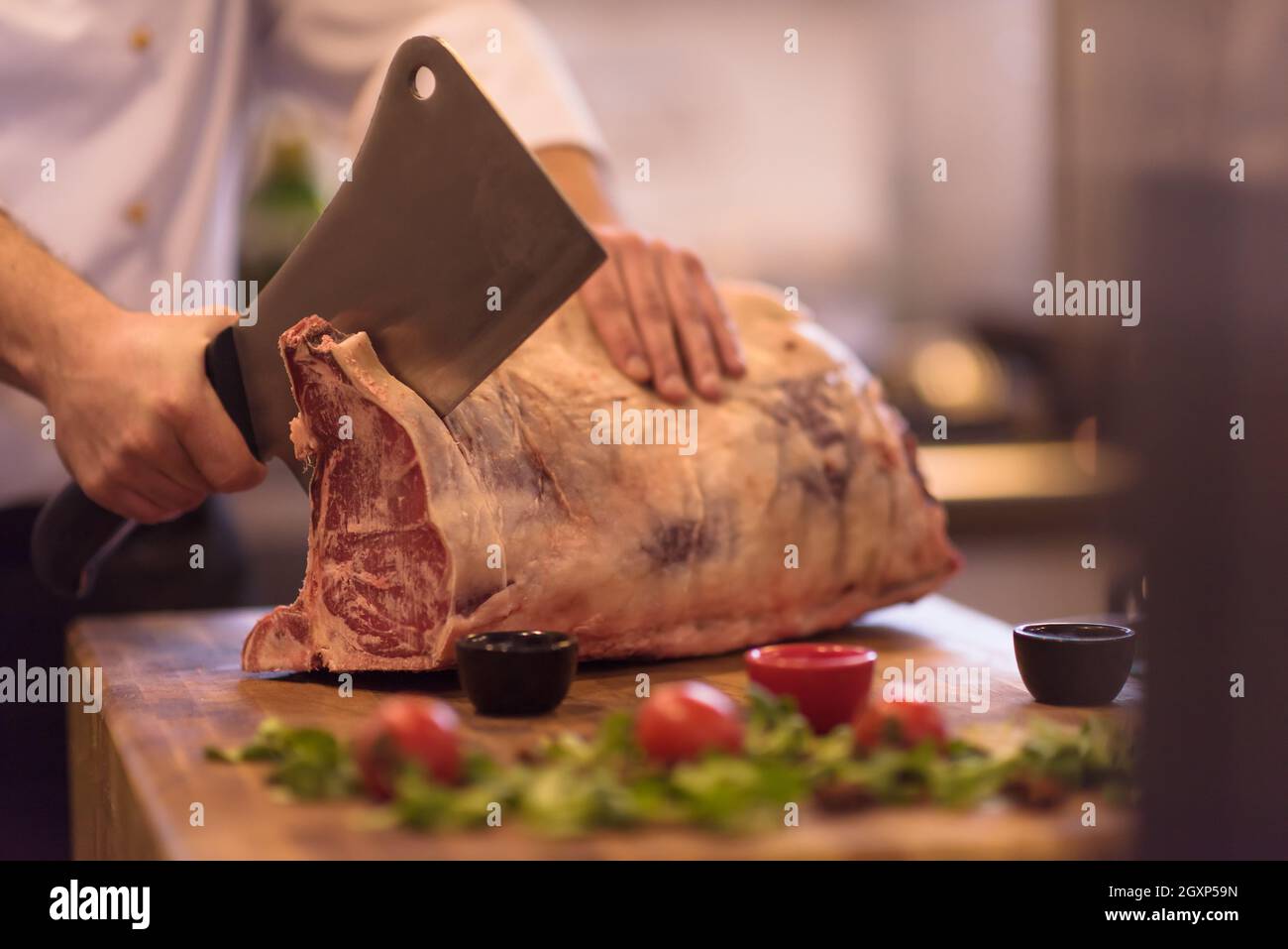 chef using ax while cutting big piece of beef on wooden board in ...