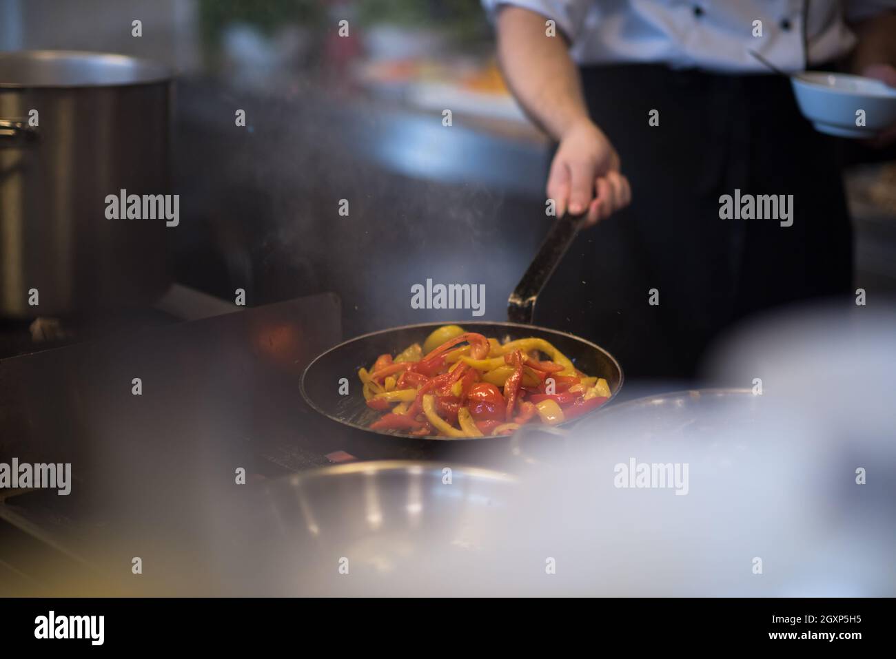 Young male chef flipping vegetables in wok at commercial kitchen Stock ...