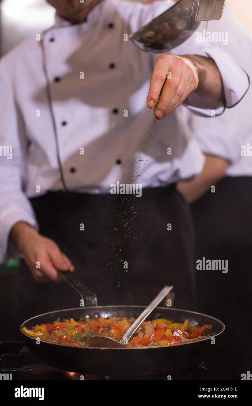 Young male chef putting spices on vegetables in wok at commercial ...