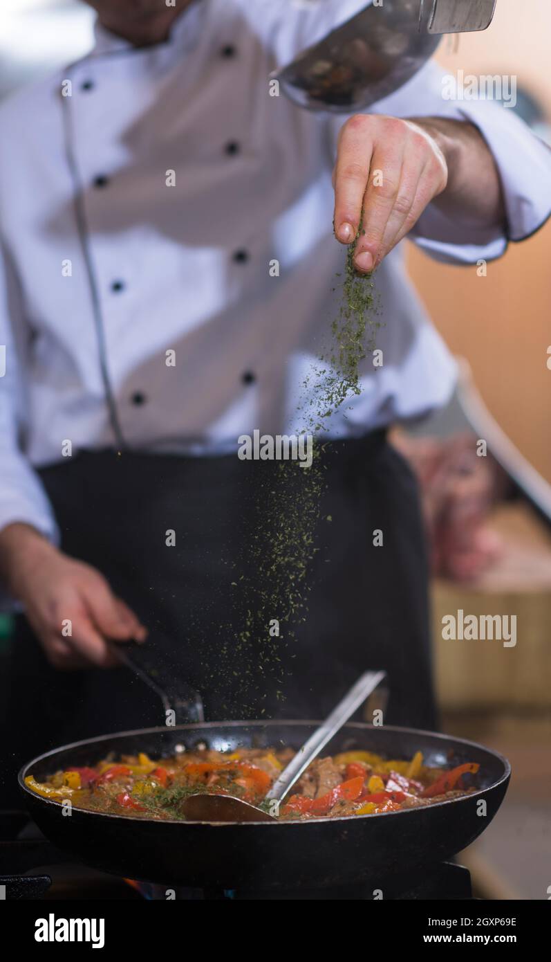 Young male chef putting spices on vegetables in wok at commercial ...