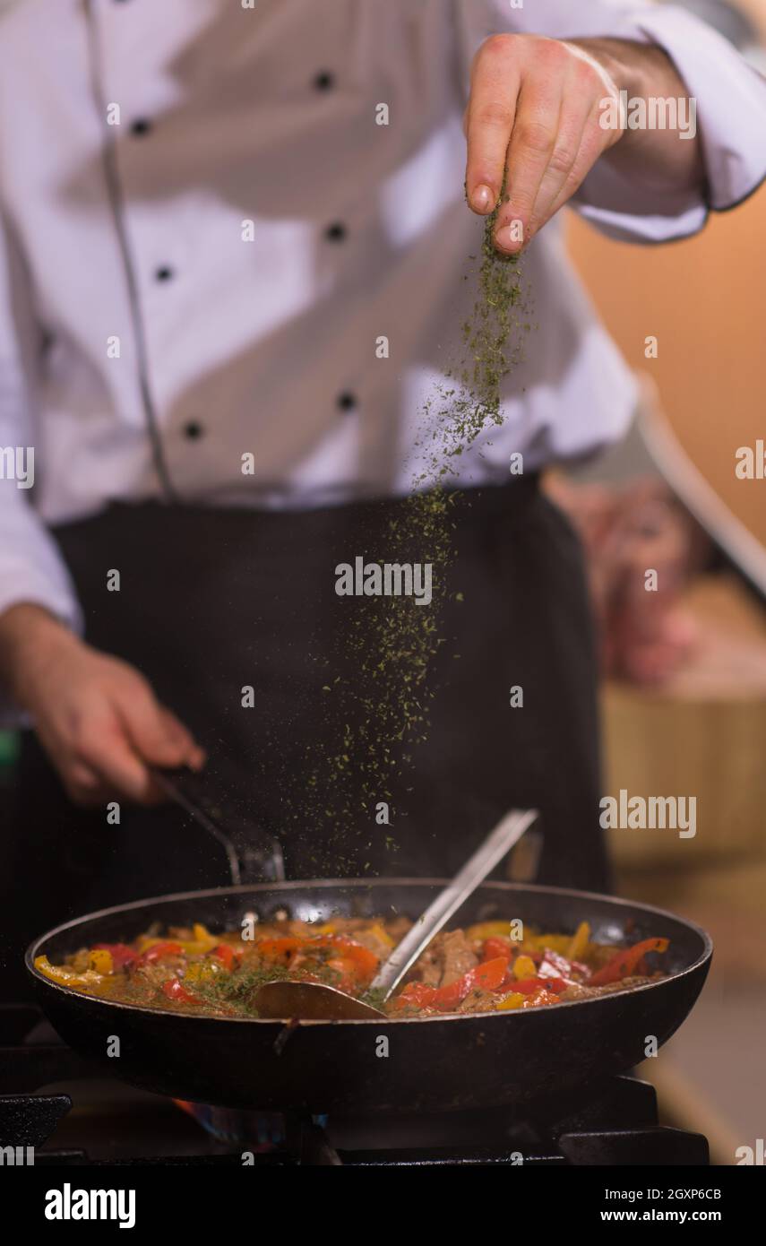 Young male chef putting spices on vegetables in wok at commercial ...