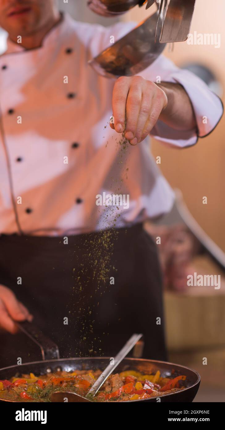 Young male chef putting spices on vegetables in wok at commercial ...