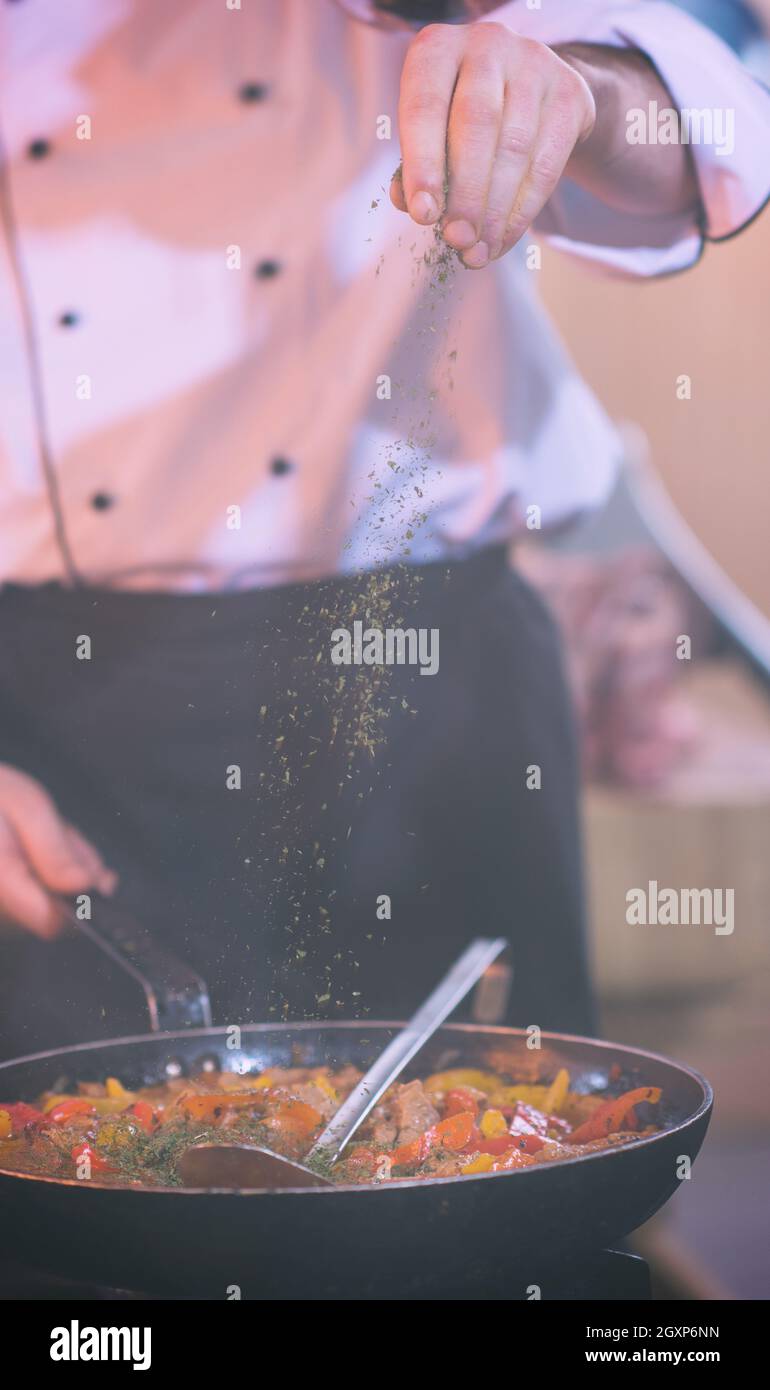 Young male chef putting spices on vegetables in wok at commercial ...