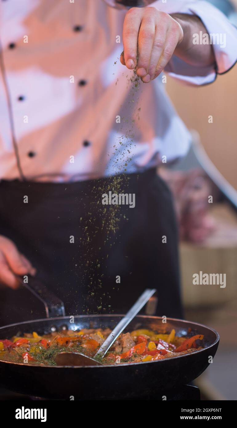 Young male chef putting spices on vegetables in wok at commercial ...