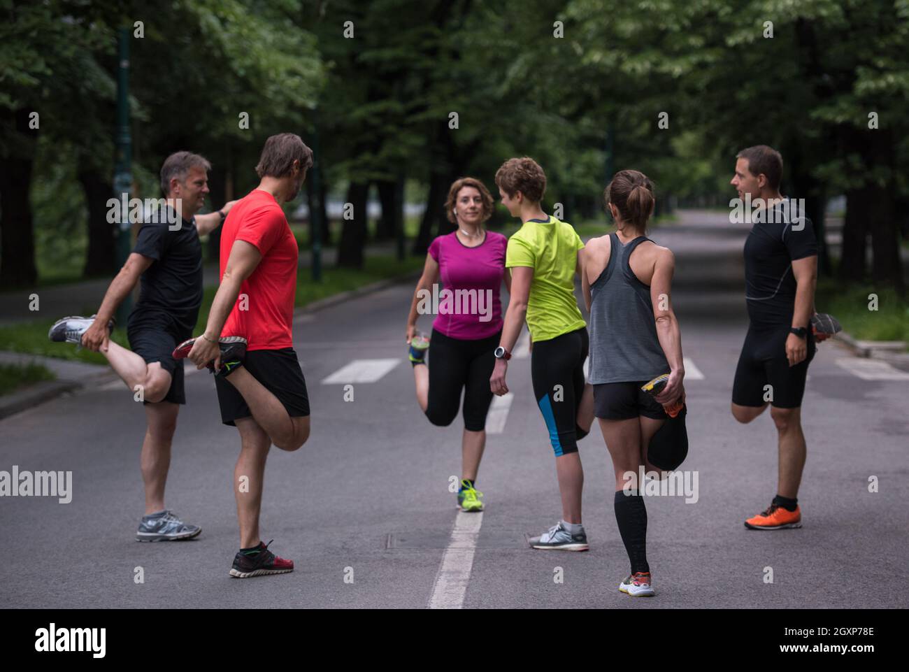 healthy runners team warming up and stretching in city park before ...