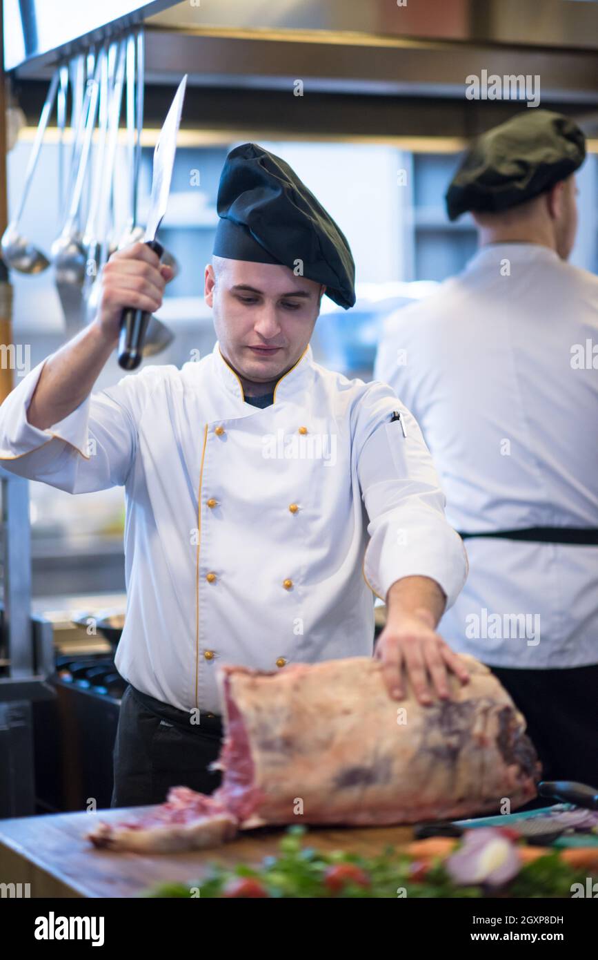 chef using ax while cutting big piece of beef on wooden board in ...