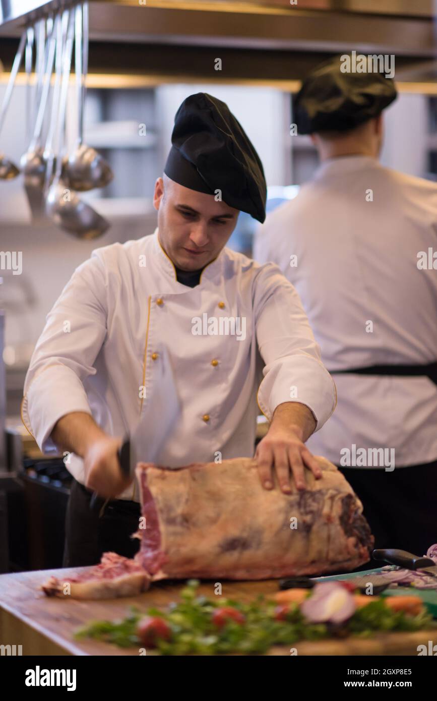 chef using ax while cutting big piece of beef on wooden board in ...