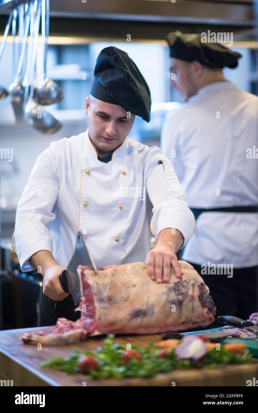 chef using ax while cutting big piece of beef on wooden board in ...