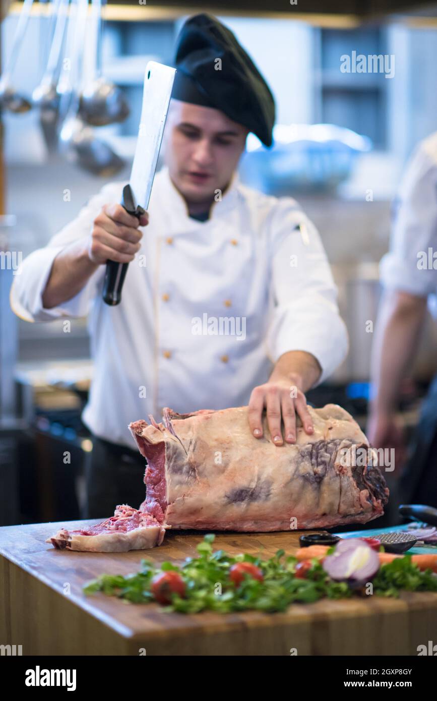 chef using ax while cutting big piece of beef on wooden board in ...