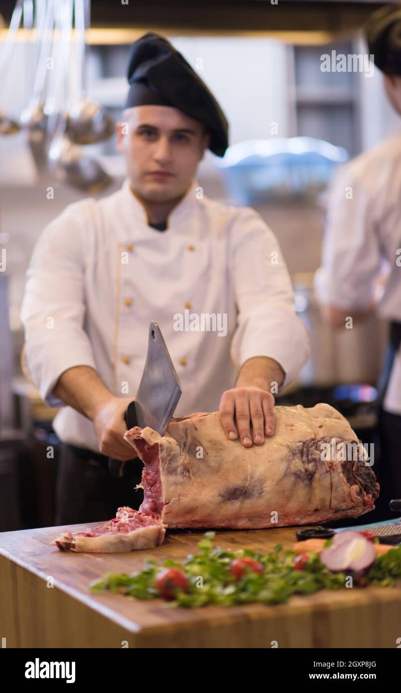 chef using ax while cutting big piece of beef on wooden board in ...