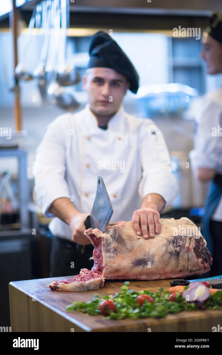 chef using ax while cutting big piece of beef on wooden board in ...