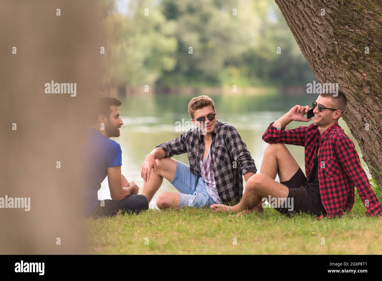Group of young men enjoying the nature sitting on the bank of the river ...