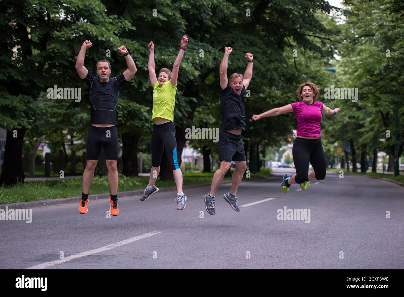 group of healthy runners team jumping in the air at city park during ...