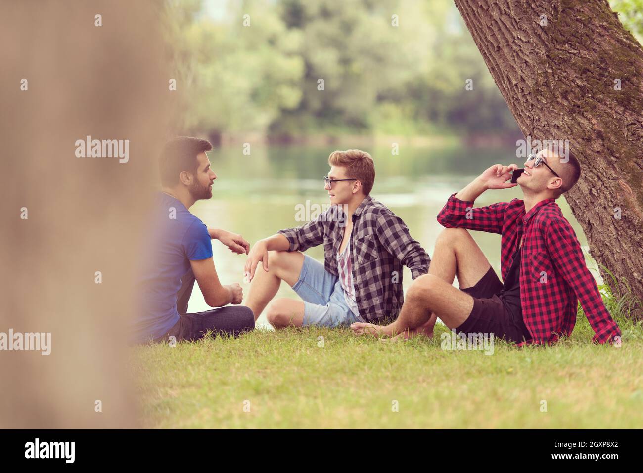 Group of young men enjoying the nature sitting on the bank of the river ...