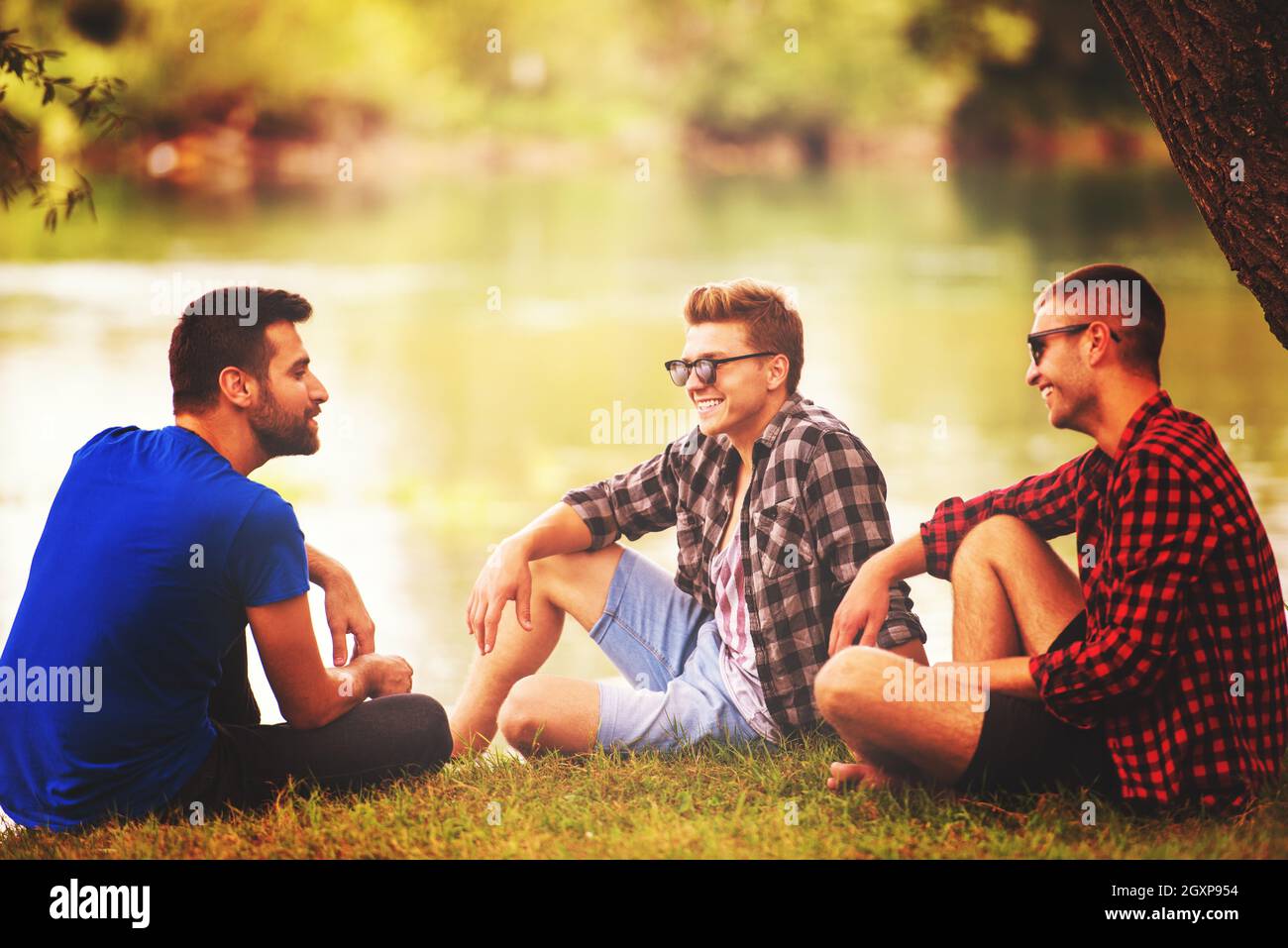 Group of young men enjoying the nature sitting on the bank of the river ...