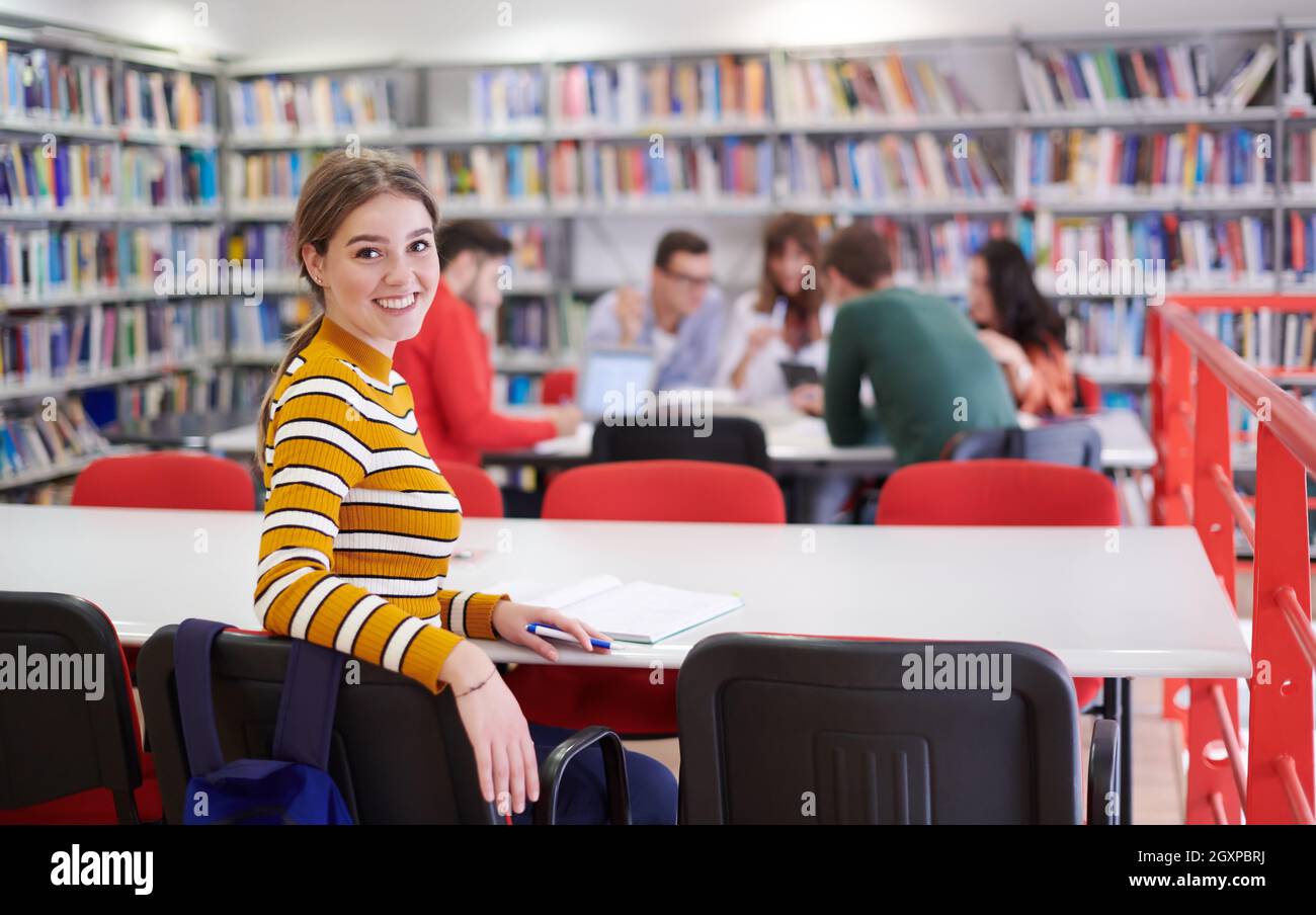 Female student taking notes from a book at library. Young woman sitting ...
