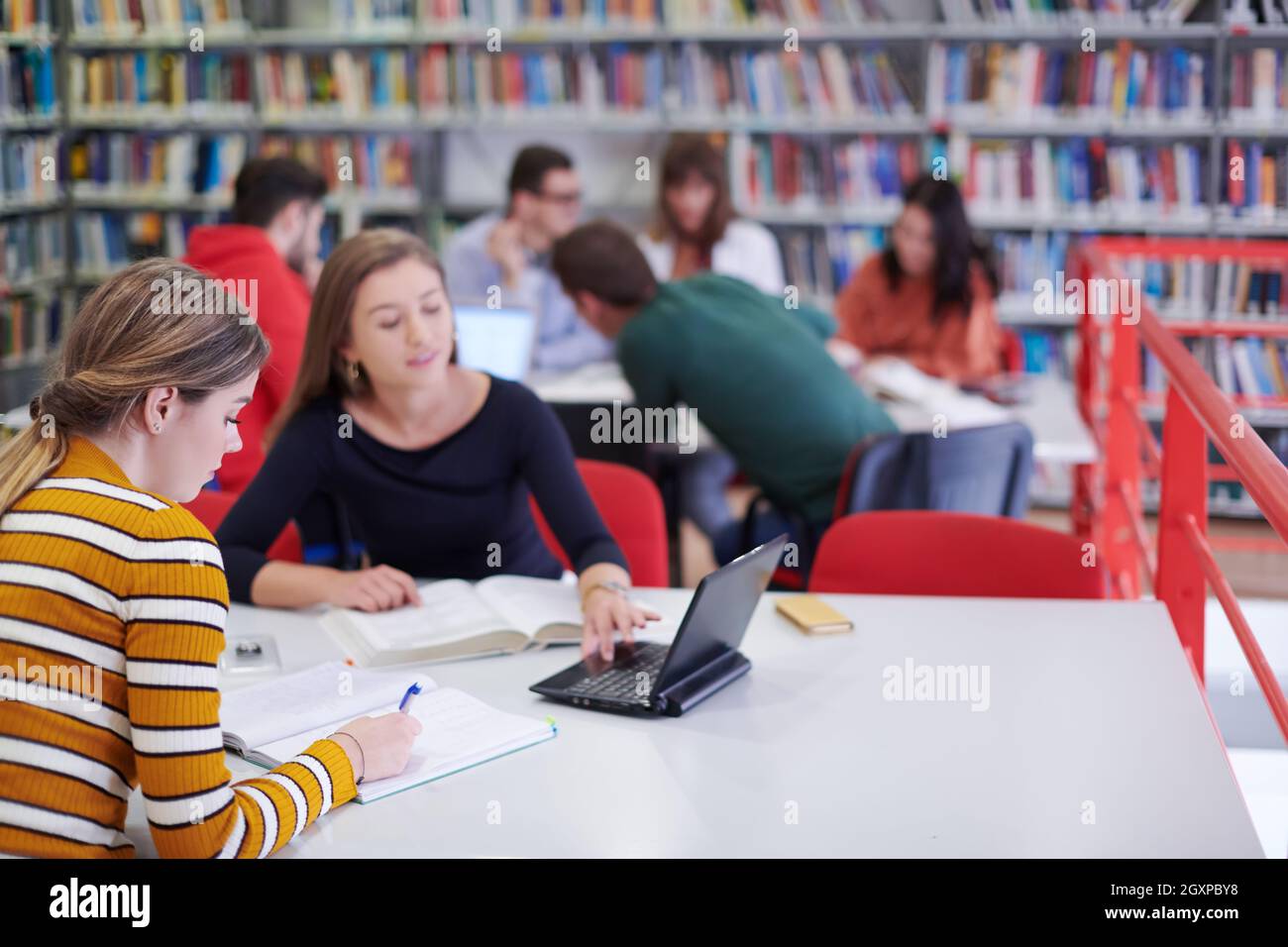 Two students taking notes from a book at library. Young two woman ...