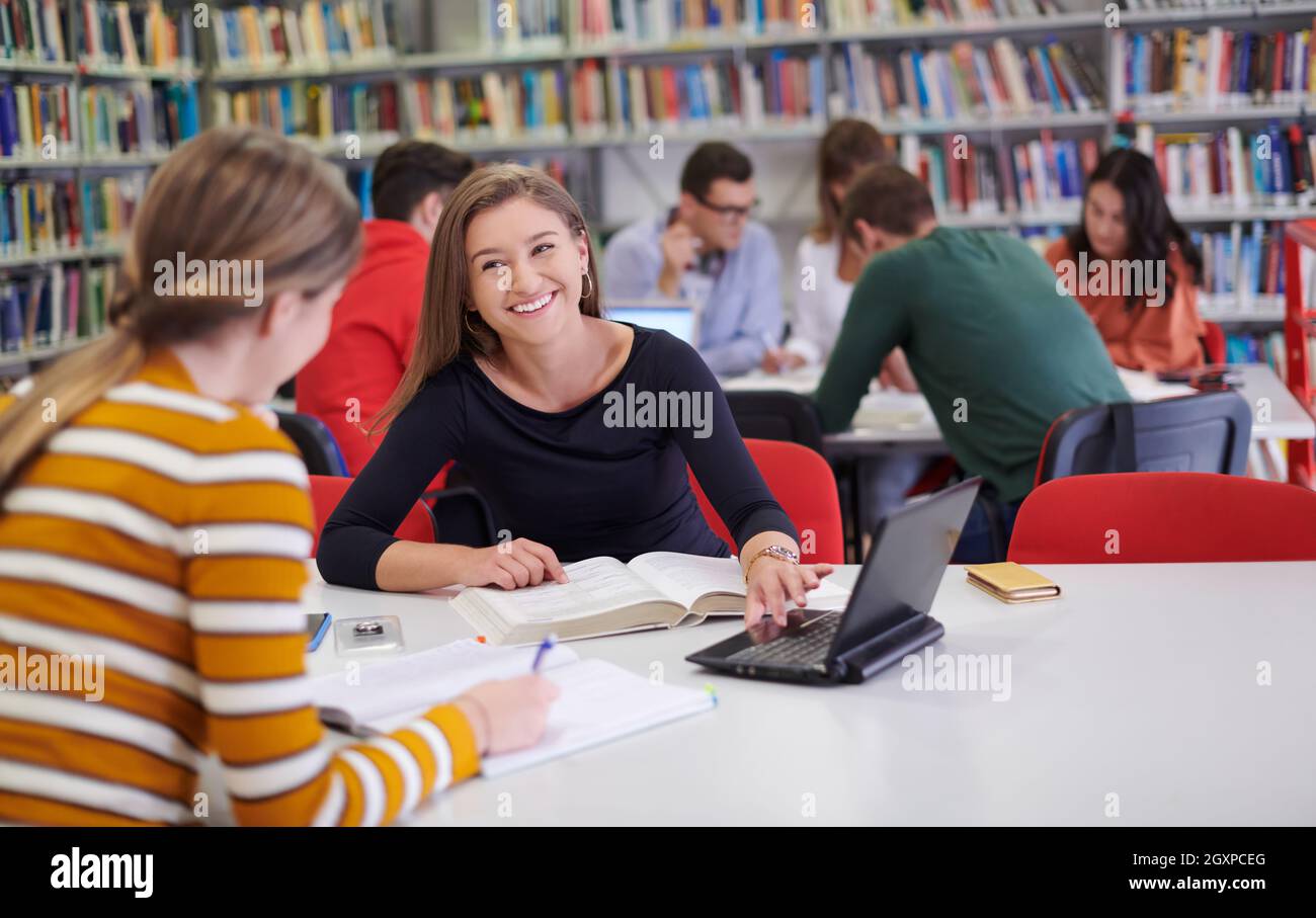Two students taking notes from a book at library. Young two woman ...
