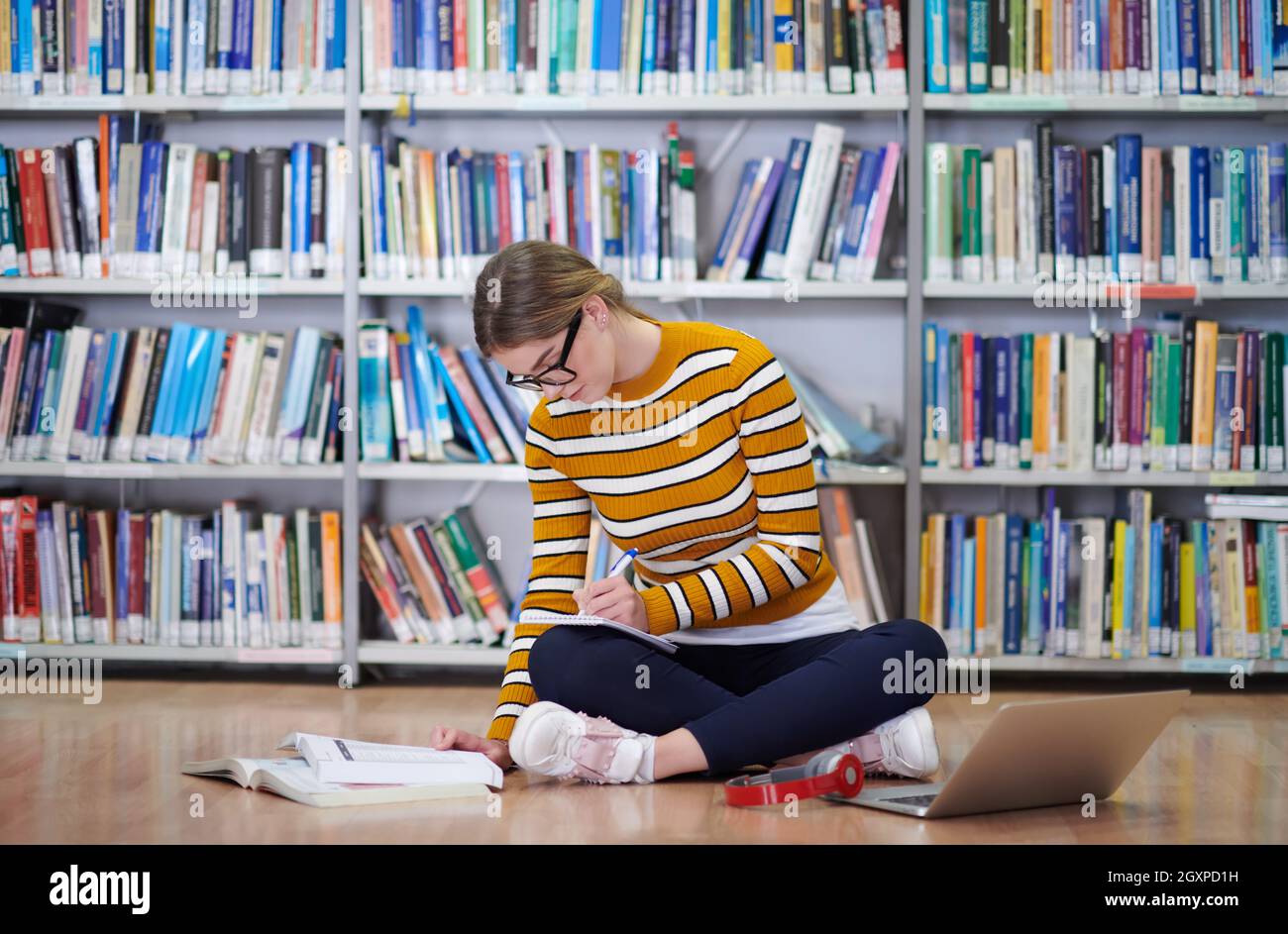 Woman student taking notes from a book at library. Young woman sitting ...