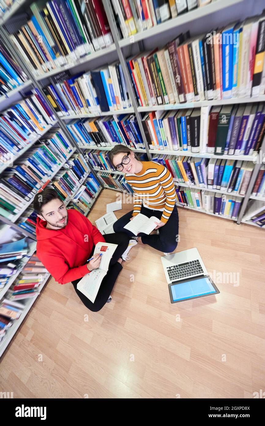 two young students sit in the school library and use a laptop to take ...