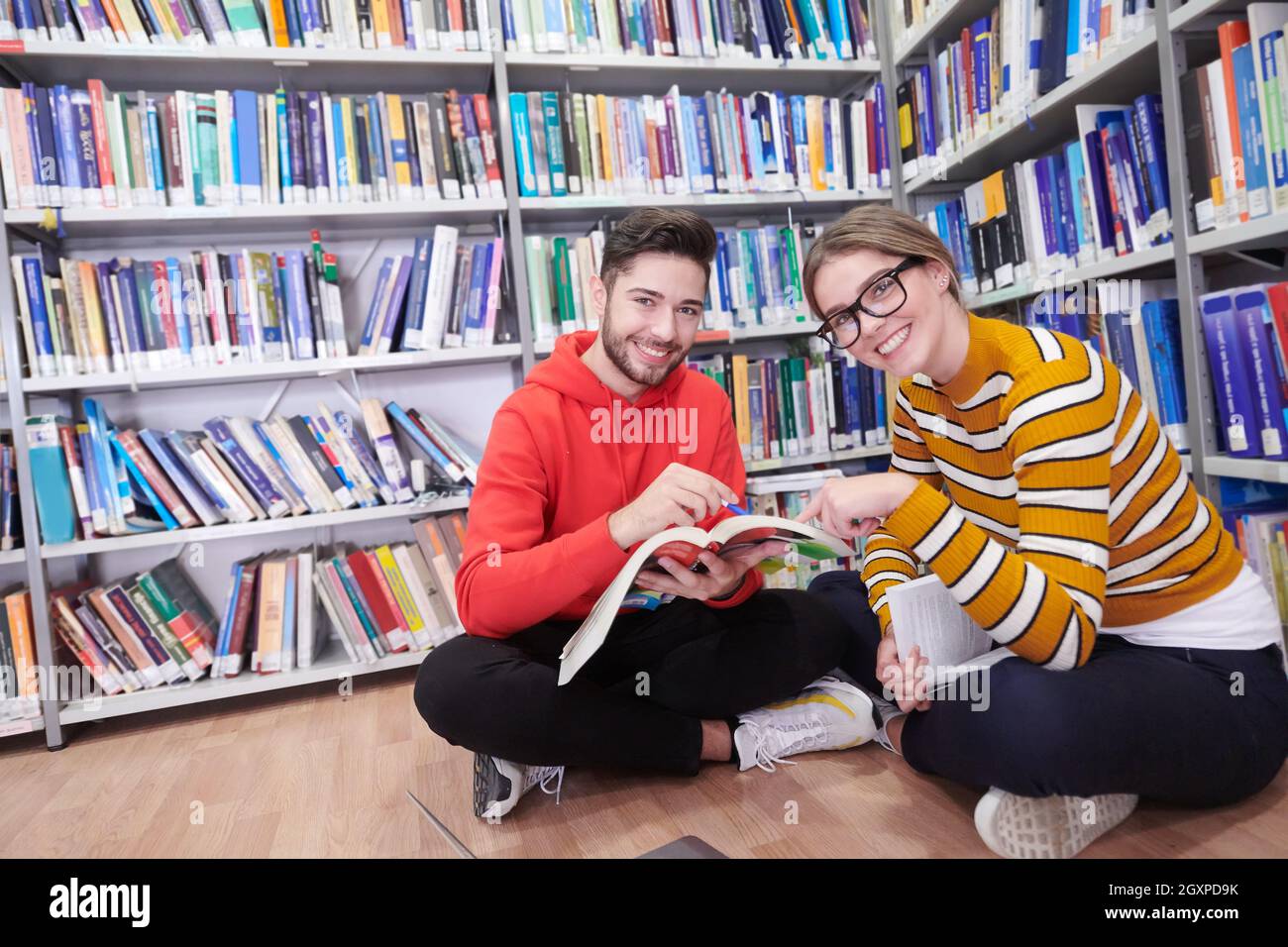two young students sit in the school library and use a laptop to take ...