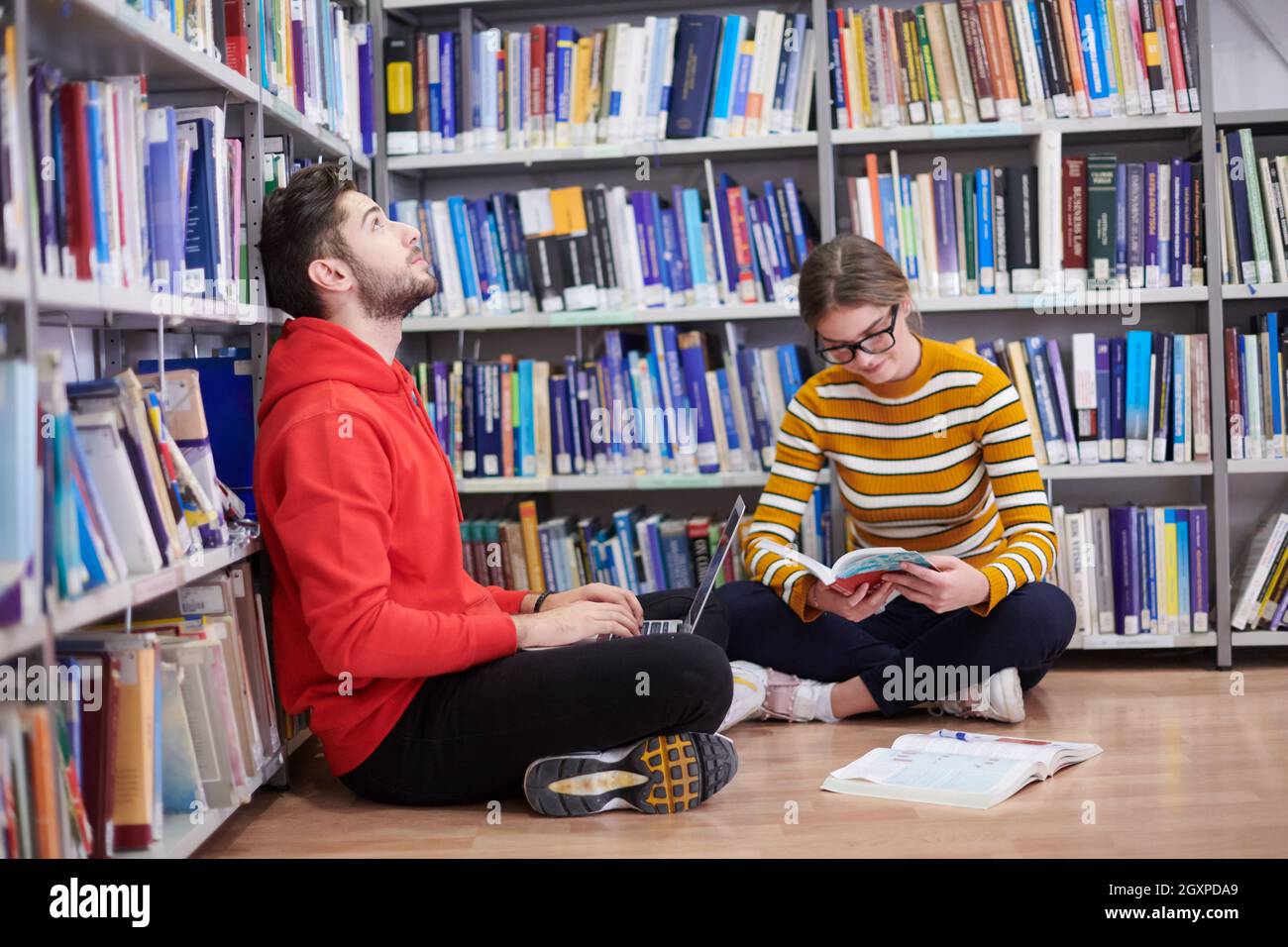 two young students sit in the school library and use a laptop to take ...