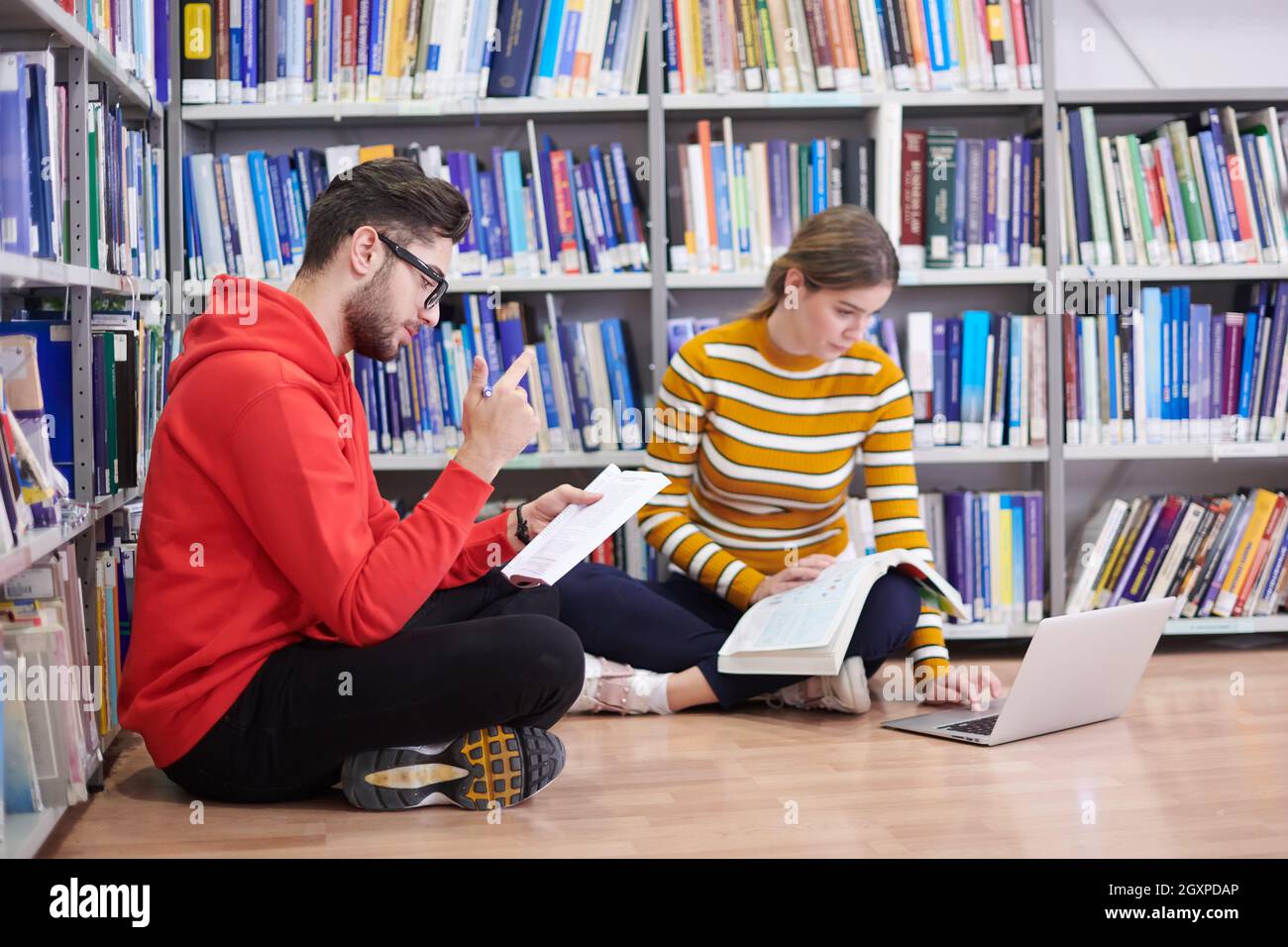two young students sit in the school library and use a laptop to take ...