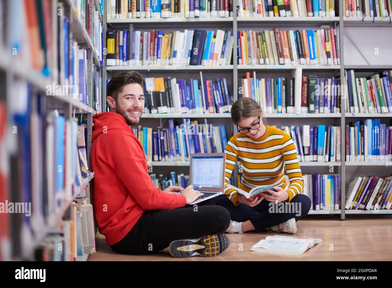 two young students sit in the school library and use a laptop to take ...