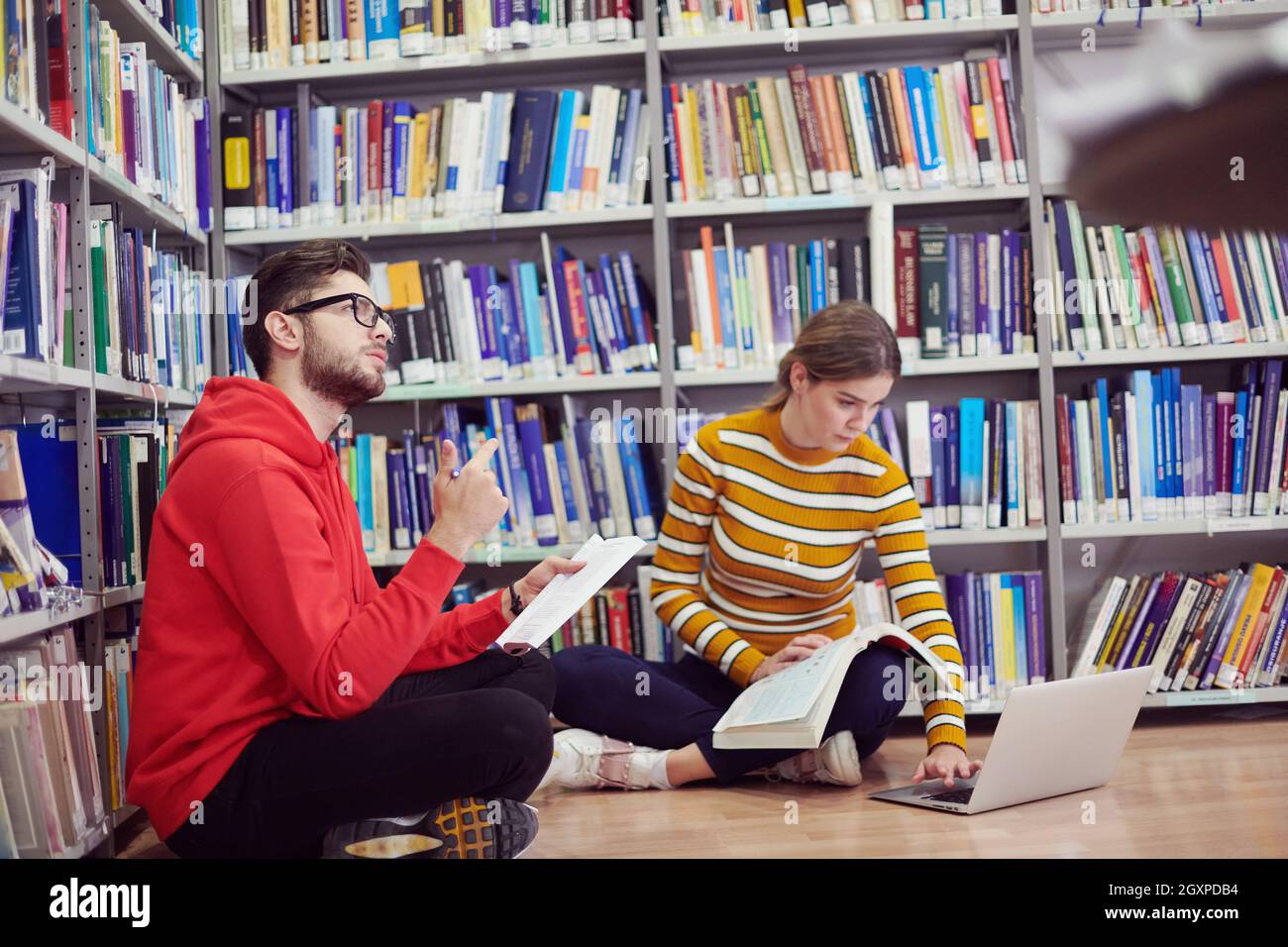 two young students sit in the school library and use a laptop to take ...