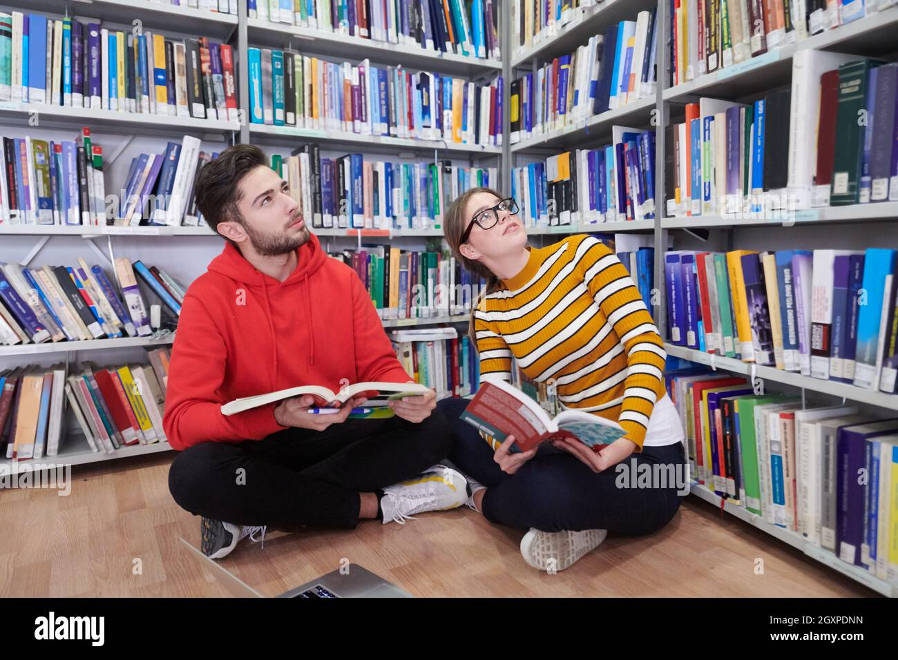 two young students sit in the school library and use a laptop to take ...