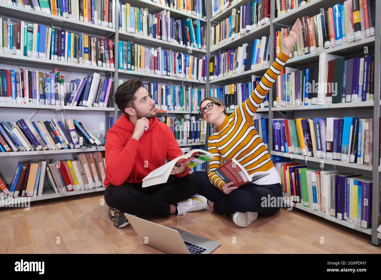 two young students sit in the school library and use a laptop to take ...
