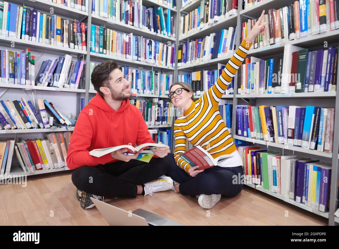 two young students sit in the school library and use a laptop to take ...