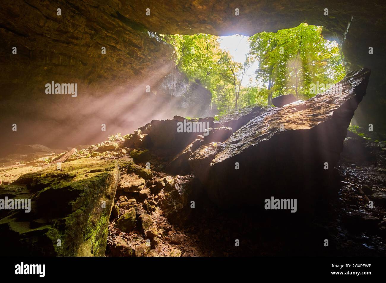 Cave opening with large rocks and beams of light through fog Stock ...