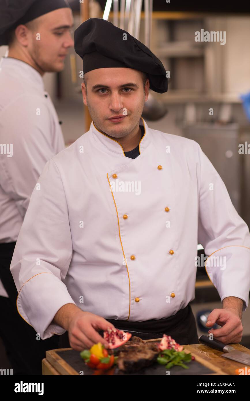 Chef in hotel or restaurant kitchen preparing beef steak with vegetable ...