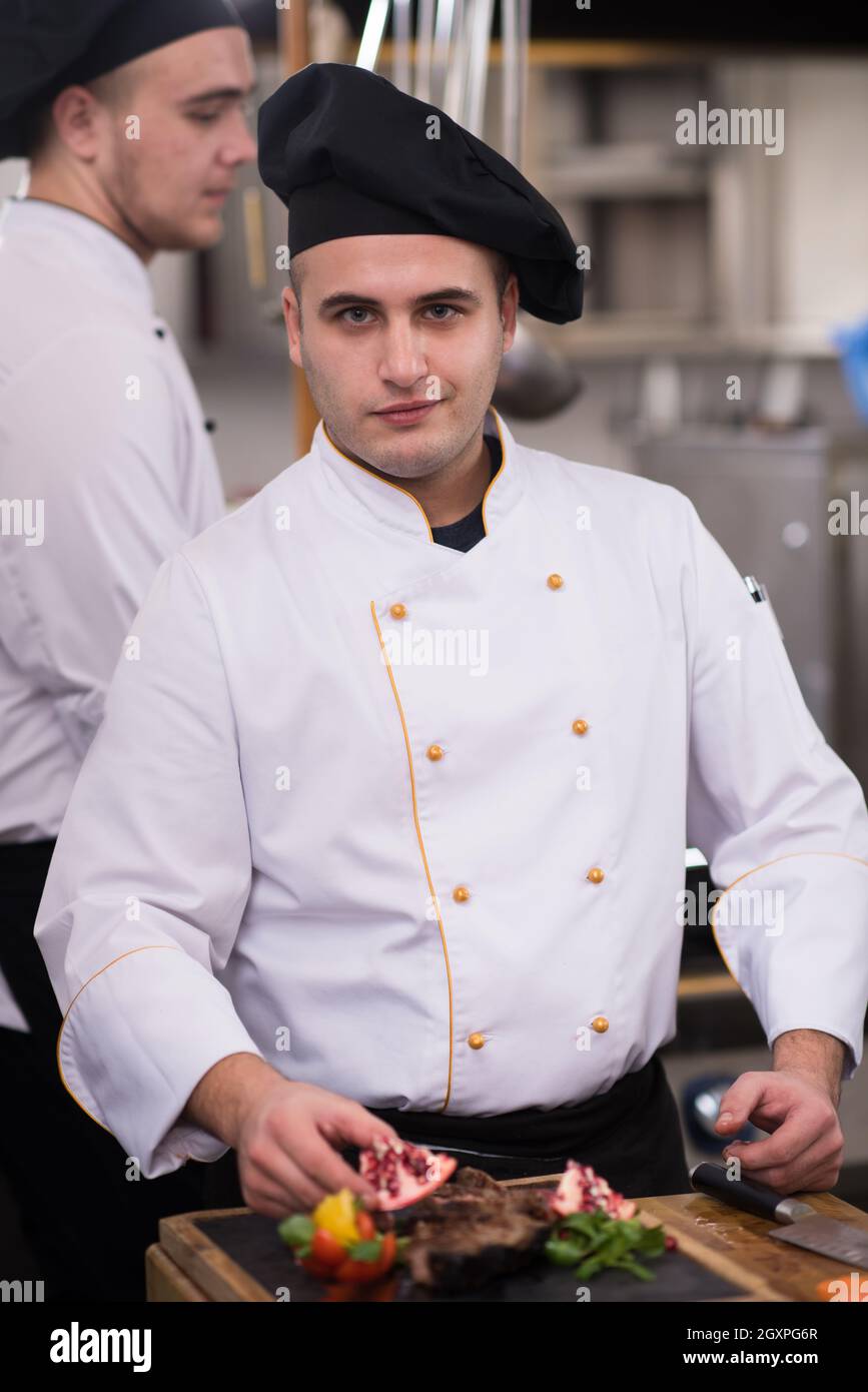 Chef in hotel or restaurant kitchen serving beef steak with vegetable ...