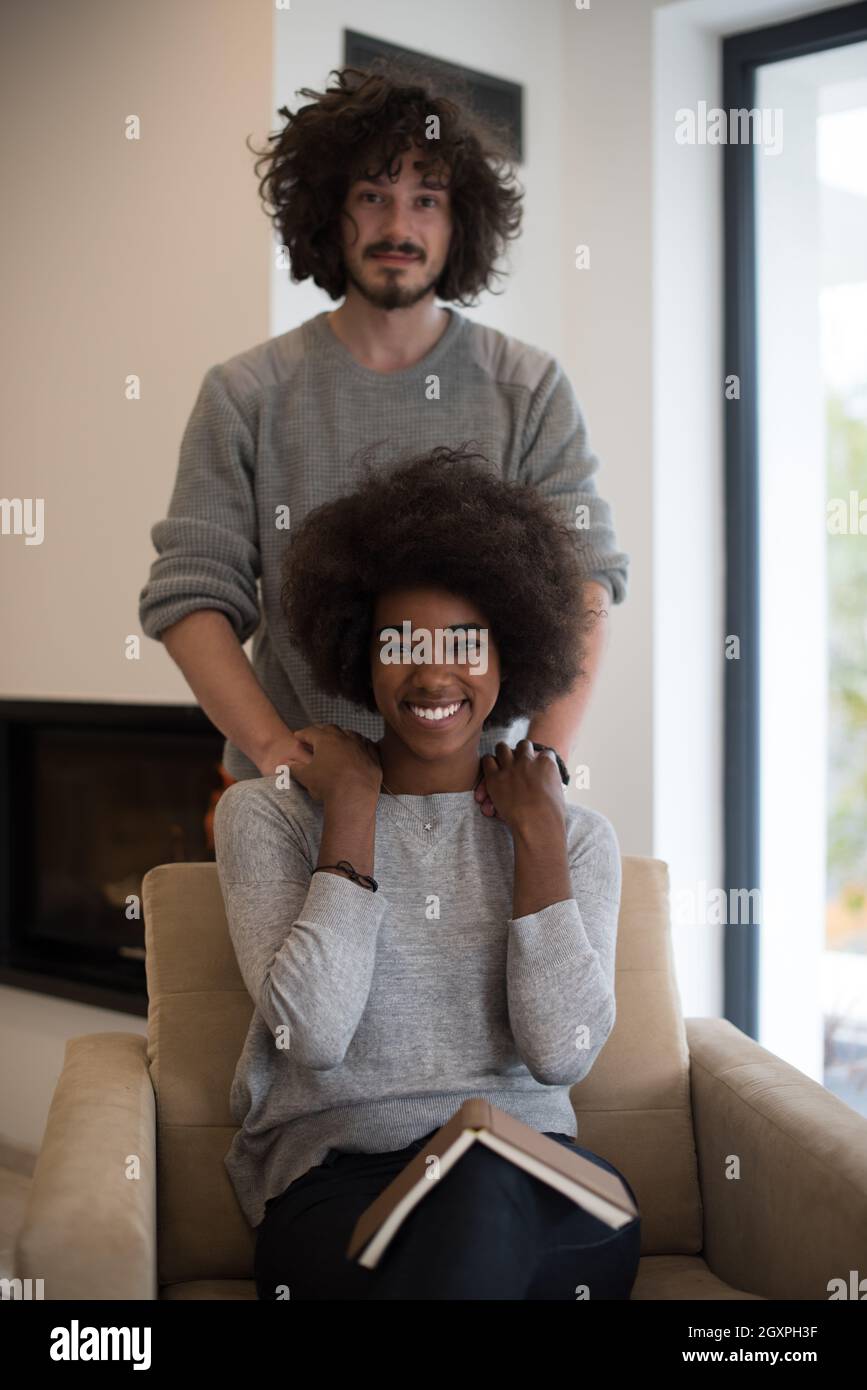Young beautiful multiethnic couple hugging in front of fireplace at home when reading a book at ...